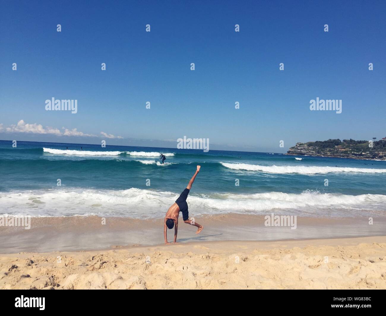 Full Length Of Shirtless Man Performing Cartwheel On Beach Against Blue ...