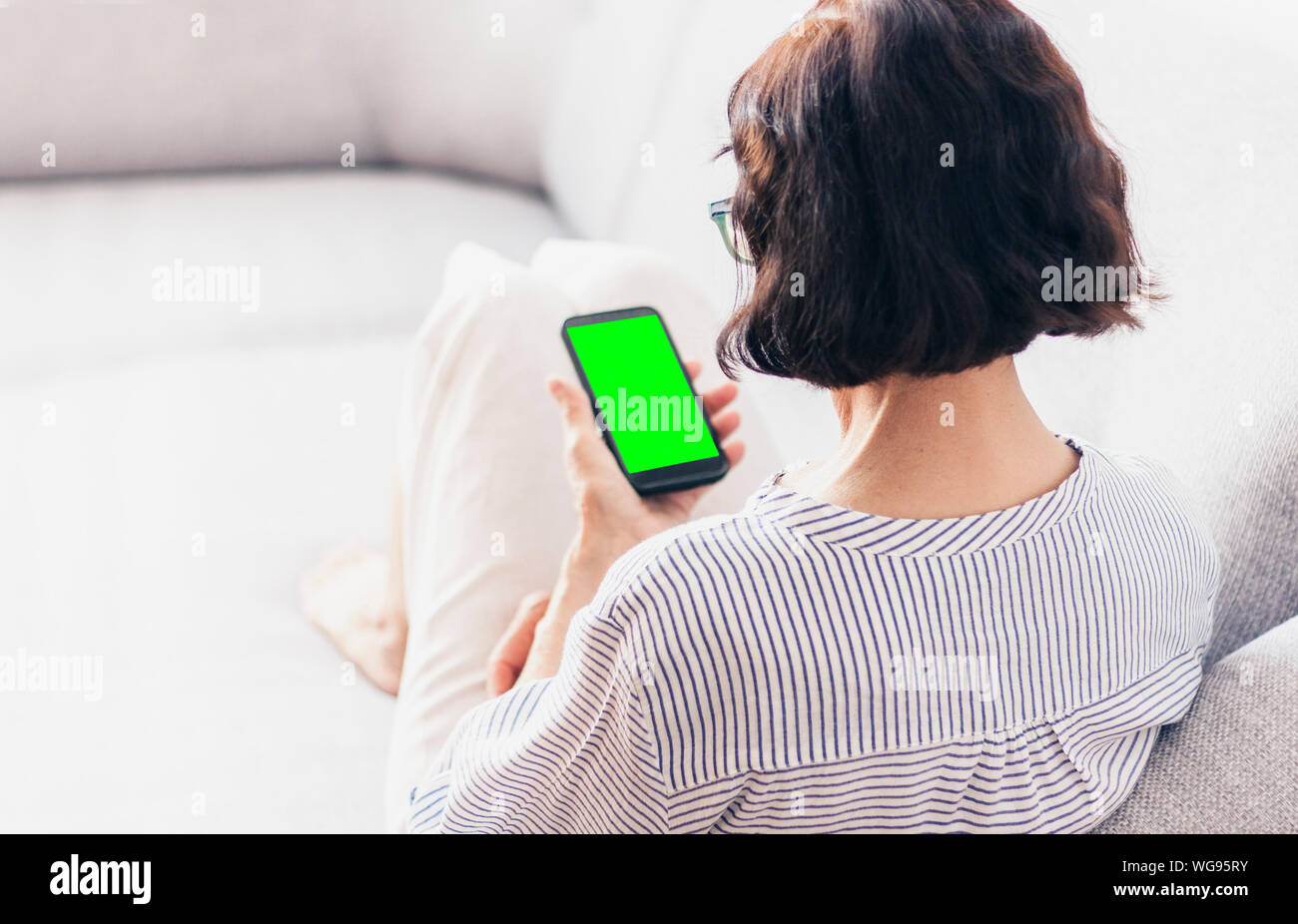Middle-aged brunette woman with glasses on the gray sofa use green screen smartphone Stock Photo ...