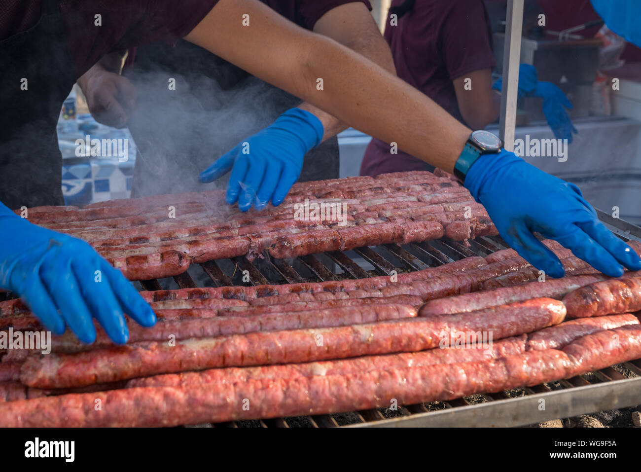BBQ Sausage lined up on a large outdoor grill with smoke coming up from ...