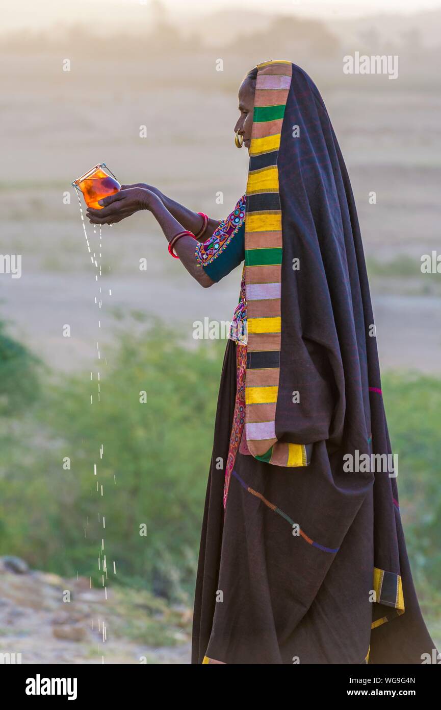 Ahir woman in traditional colorful clothes pouring water at sunet ...