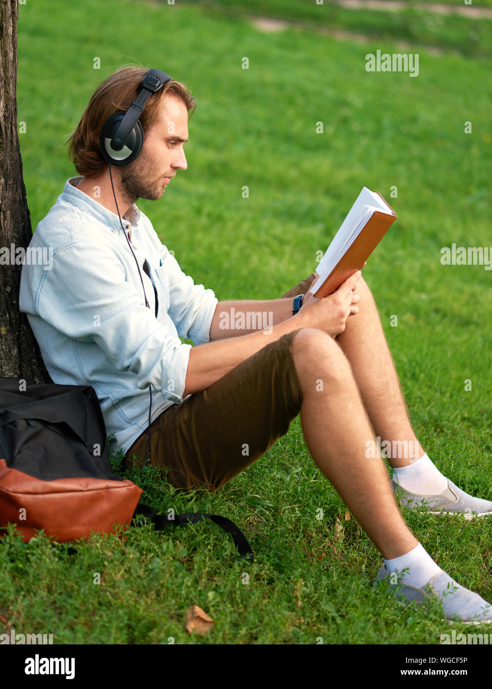 Student with headphones in park of campus read a book Stock Photo - Alamy