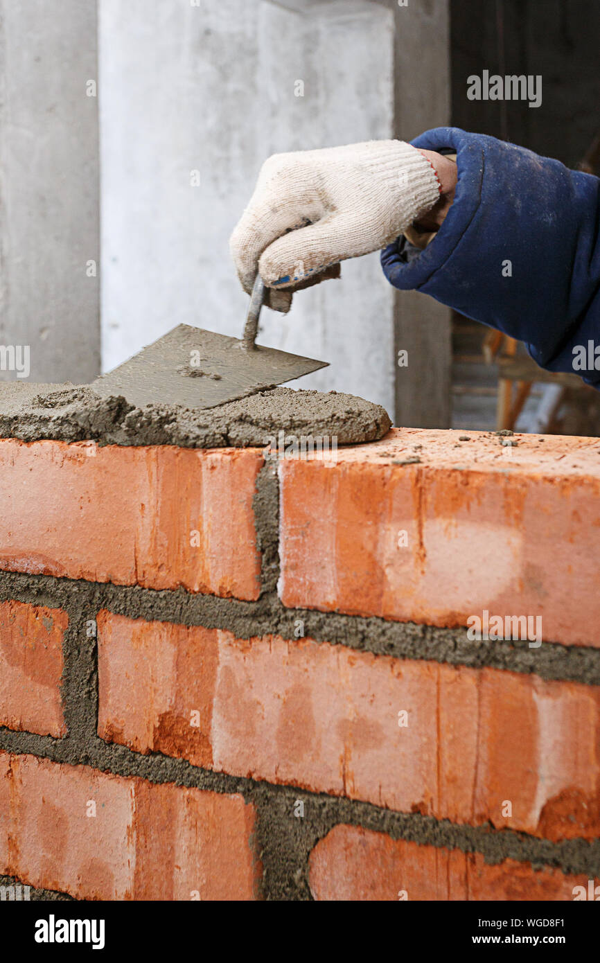 Hand in the process of laying a wall of red brick Stock Photo - Alamy