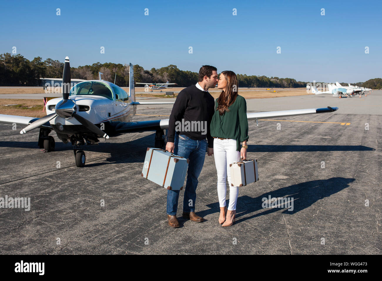 Young couple kissing as they walk away from private plane with luggage ...