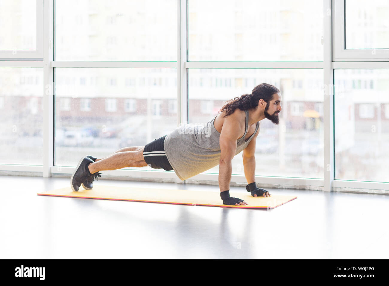 Young adult sporty muscular man with curly long hair practicing yoga ...