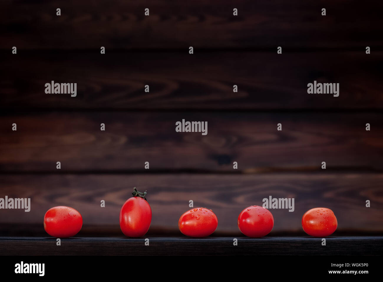 Five small bright red tomatoes in a row with one leader. Side view ...
