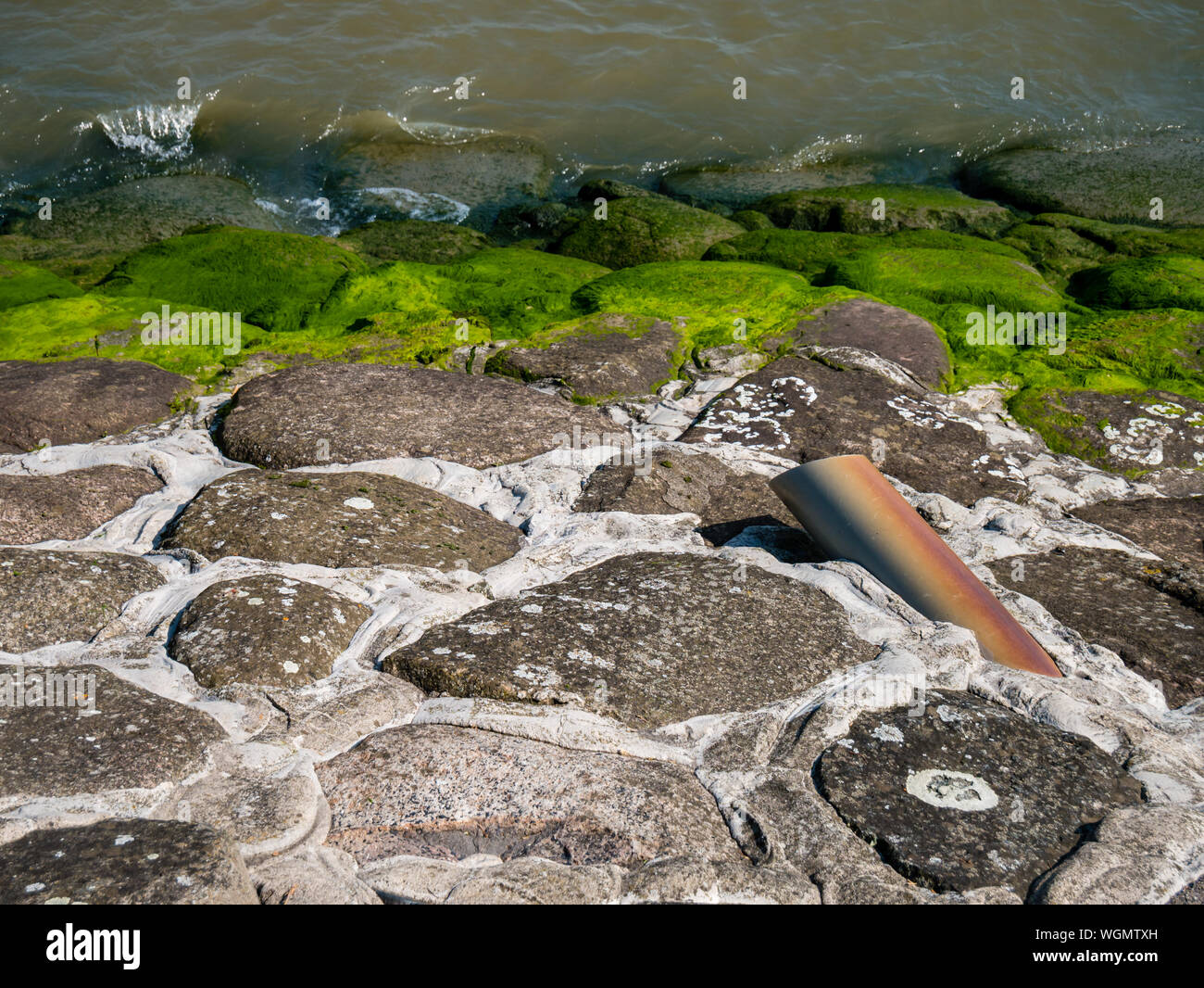 Mouth of a sewage channel at dike made of stone above waterline of a ...