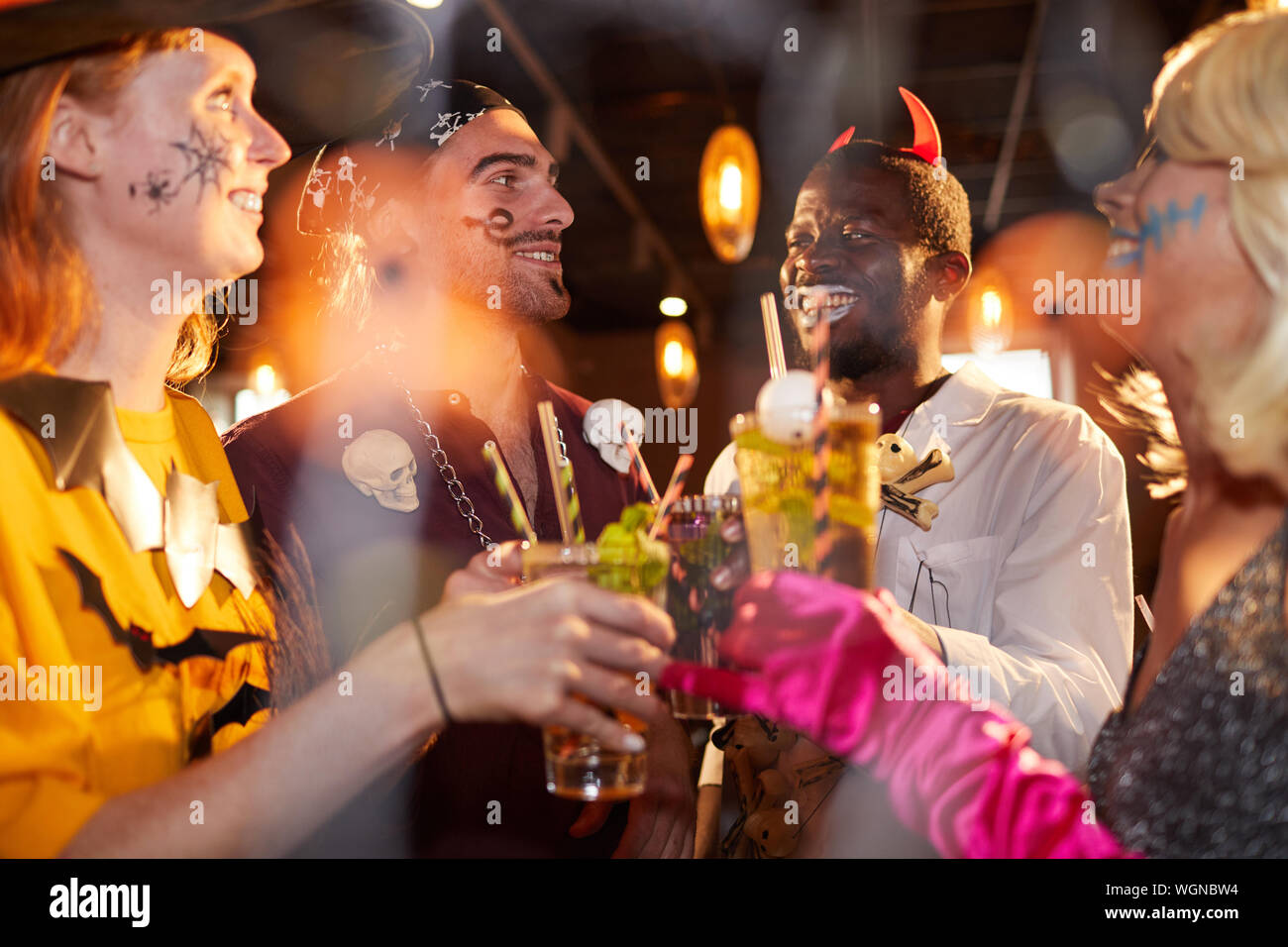 Multi-ethnic group of friends wearing Halloween costumes drinking ...