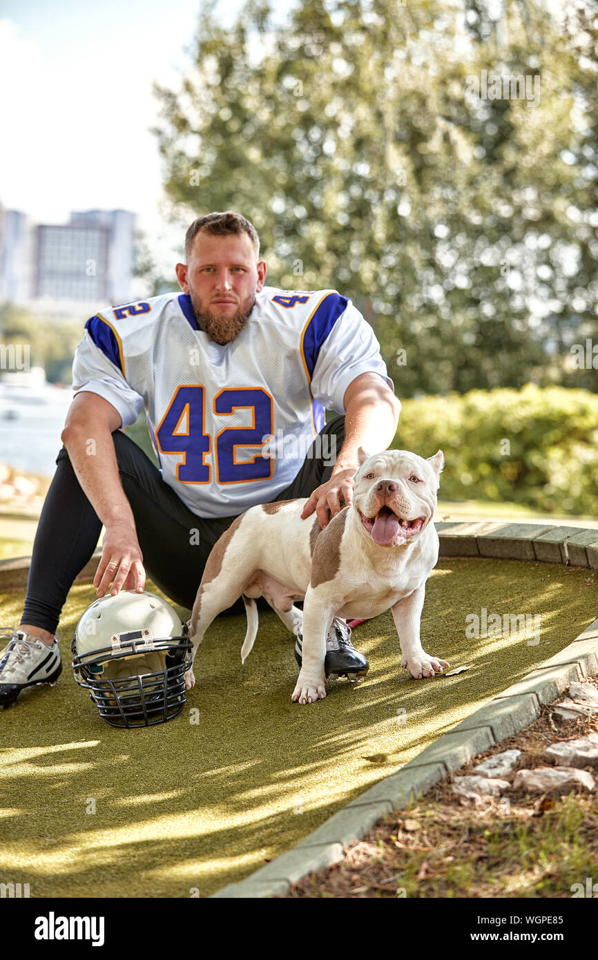 American football player with a dog posing on camera in a park. Copy ...