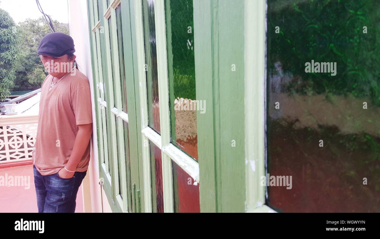 Thoughtful Mid Adult Man Standing By Window In Balcony Stock Photo - Alamy