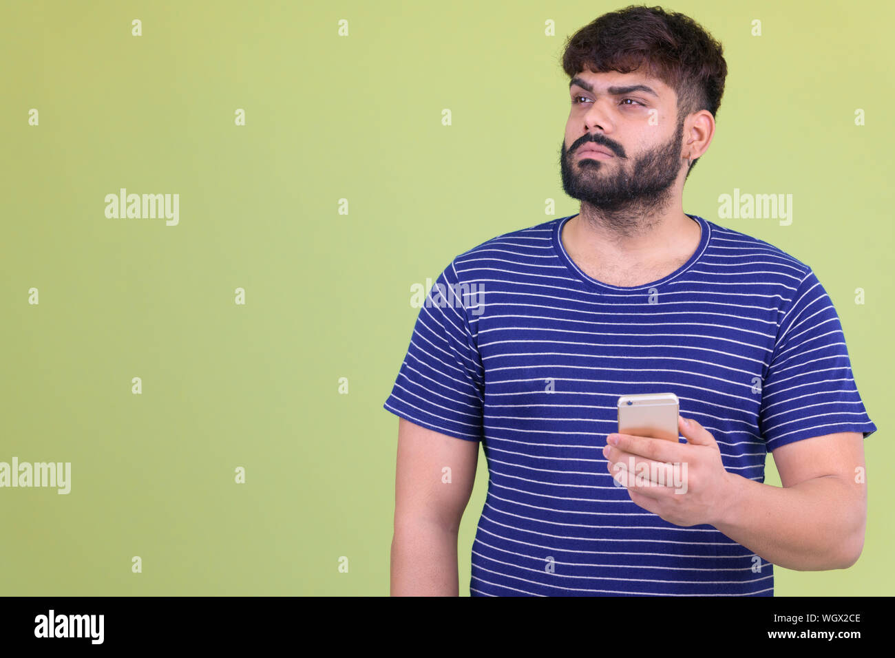 Young overweight bearded Indian man thinking while using phone Stock ...