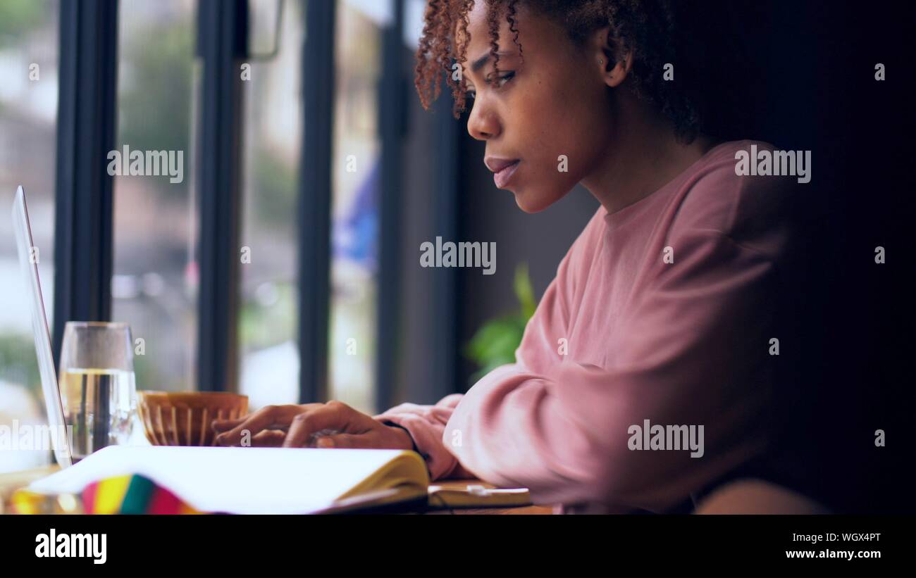 Side view of one young African woman using laptop indoor, Pretty Black ...