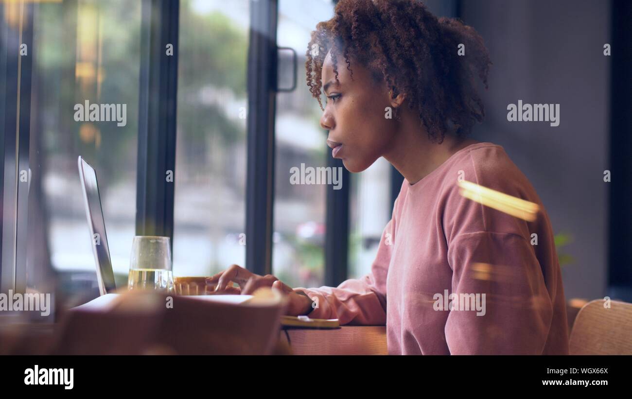 Side view of one young African woman using laptop indoor, Pretty Black ...