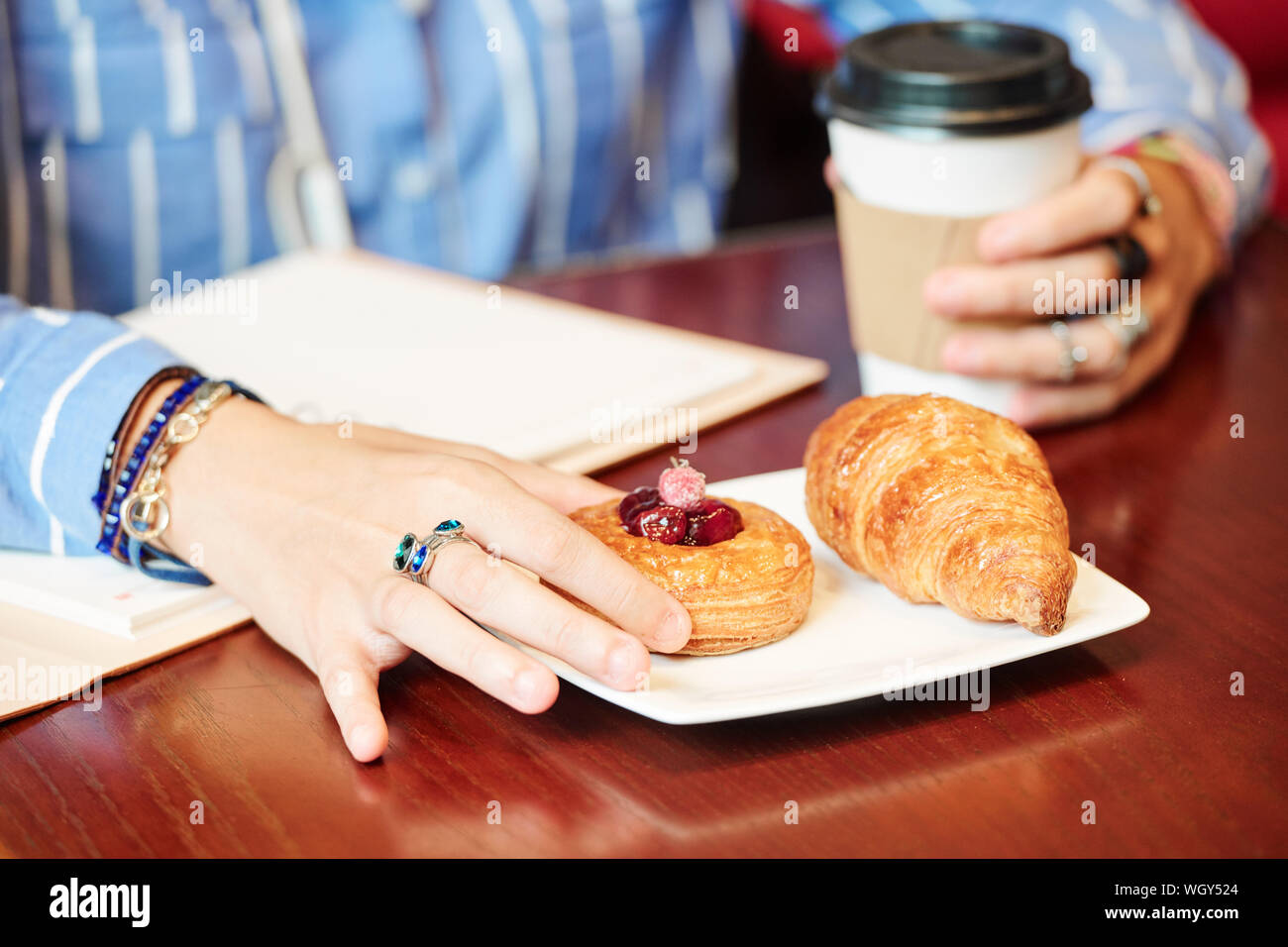 Hands of woman taking puff with cherry filling from the plate in front ...