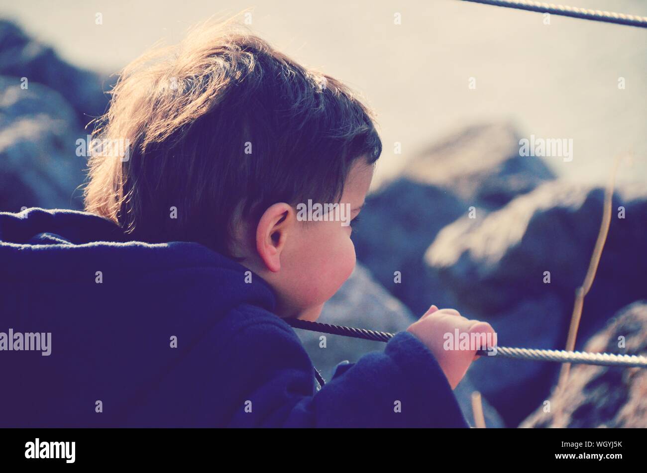 Boy Leaning On Rope By Rocks At Beach Stock Photo - Alamy