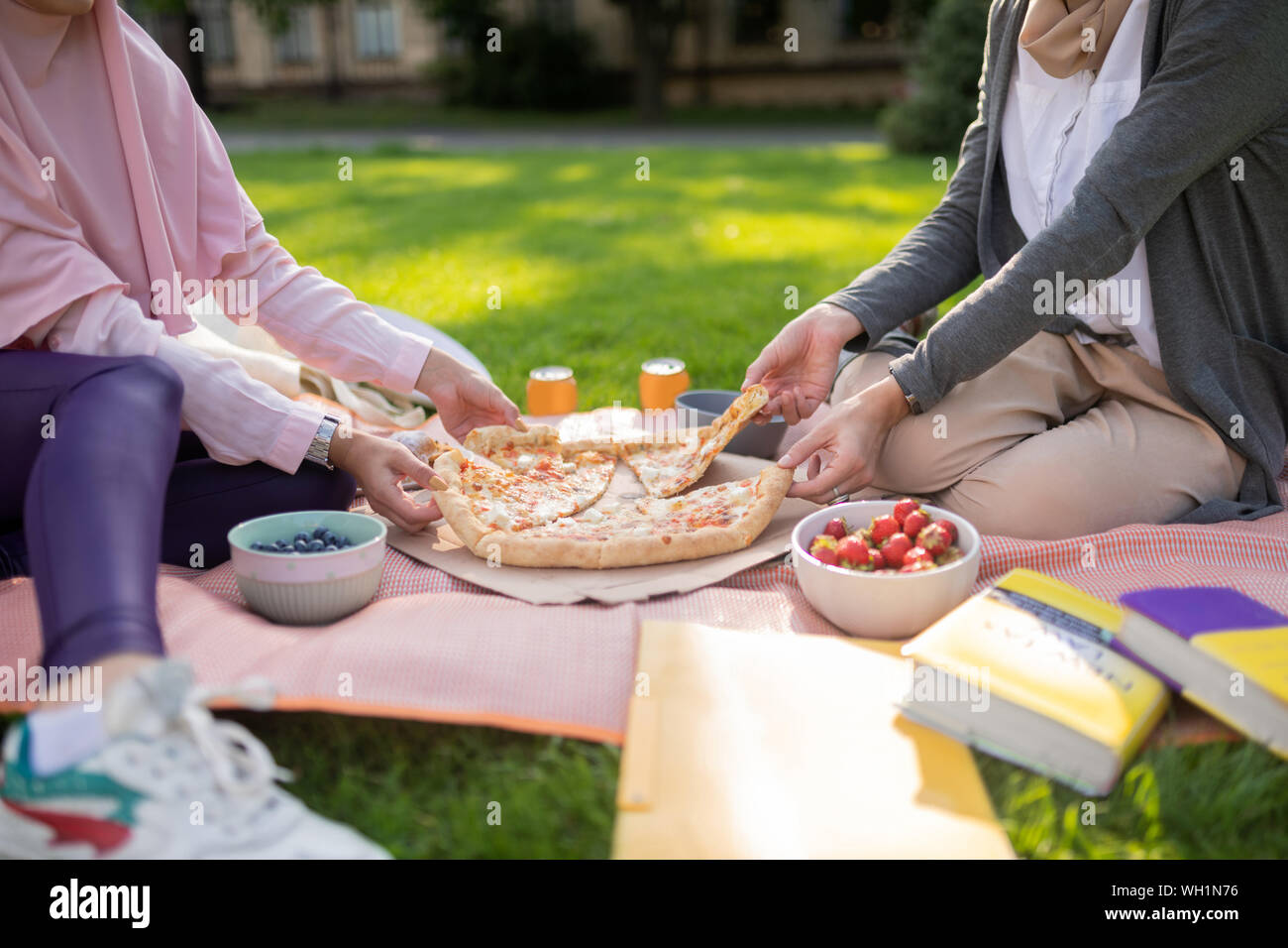 Two students sharing cheesy pizza while eating lunch outside Stock ...