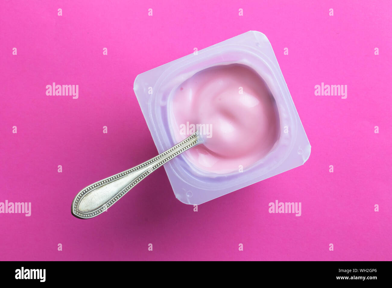 Yogurt cup with pink yoghurt and spoon on bright pink background, top ...