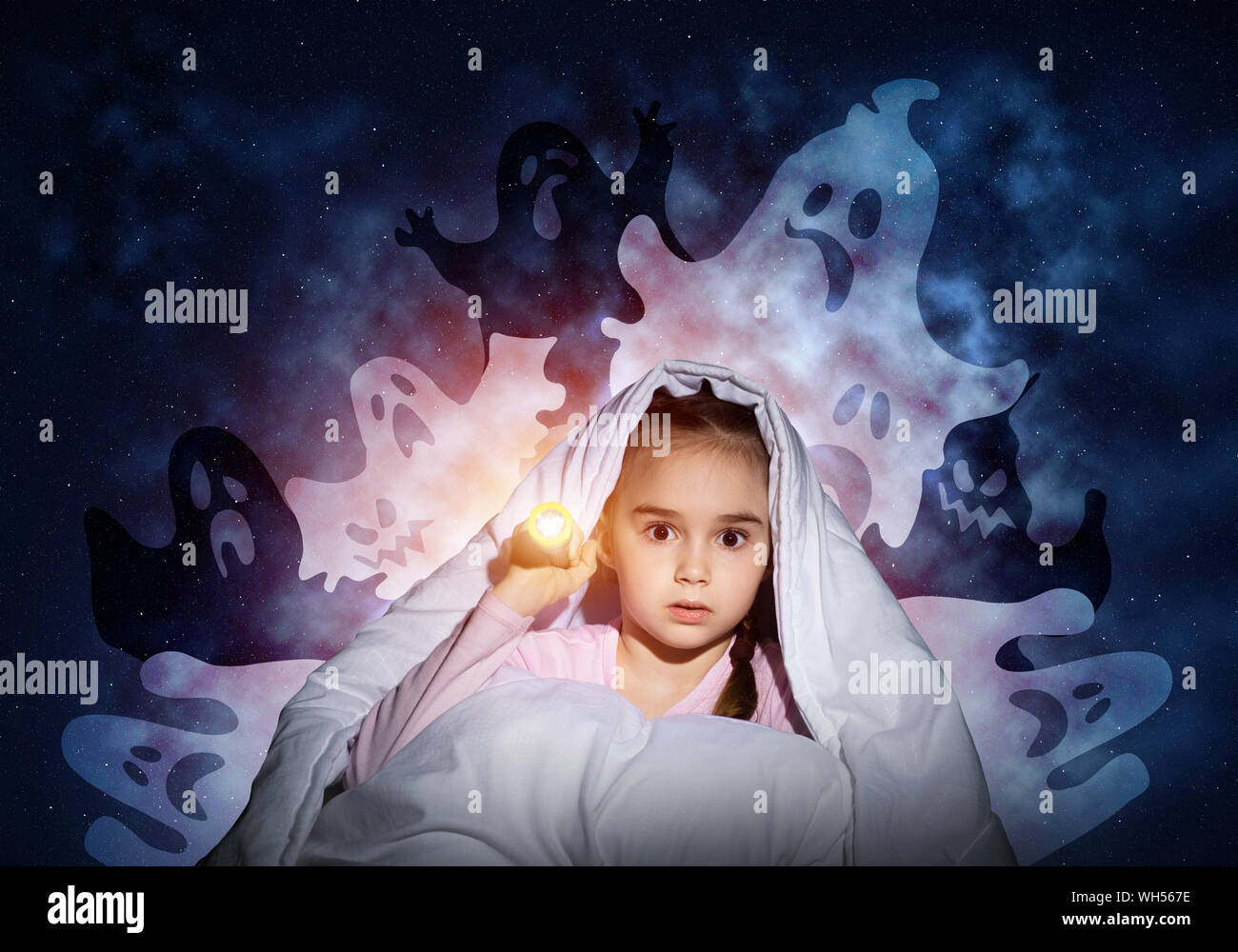 Scared girl with flashlight hiding under blanket from imaginary ghosts ...