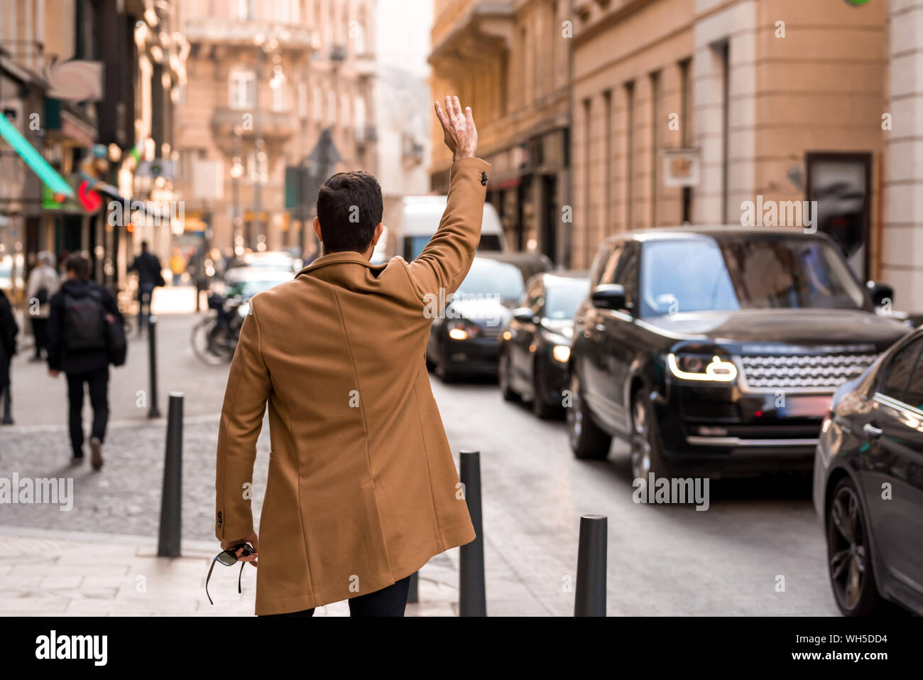 A handsome elegant man walking on the streets and waving with his hand ...