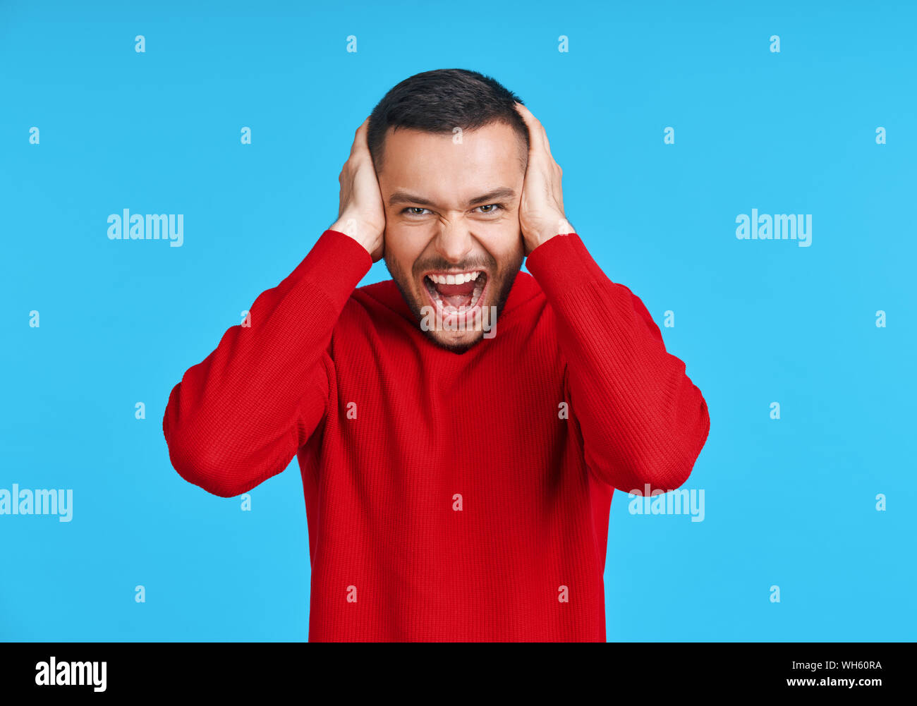 Stressed emotional young man screaming and closing ears by his hands ...