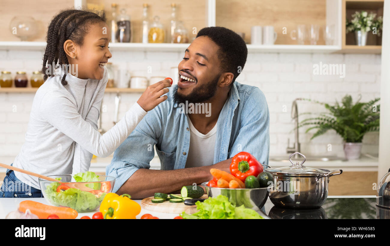 Lovely afro girl giving her dad tomato to taste Stock Photo - Alamy