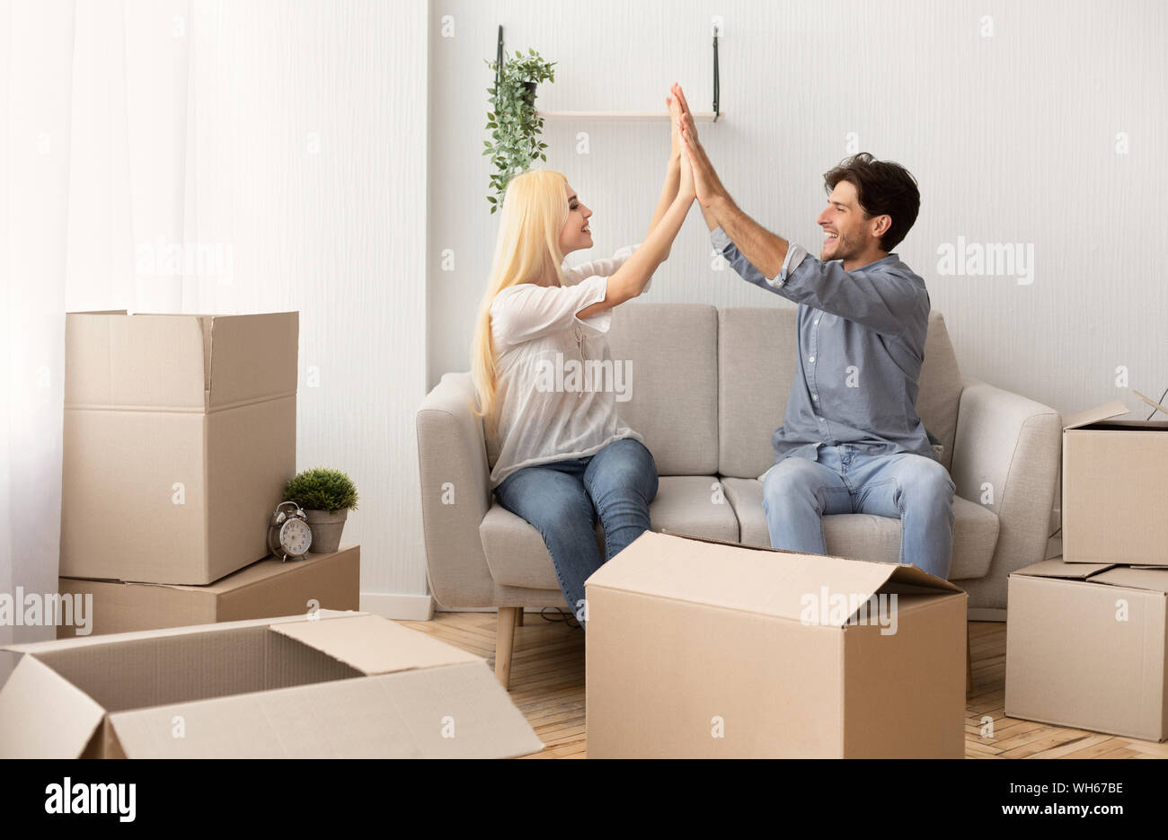 Happy Couple Giving High-Five Sitting On Couch Among Moving Boxes Stock ...