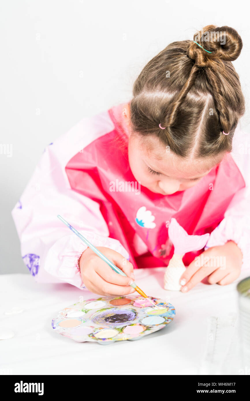 Little girl painting mermaid tails made out of modeling clay with ...