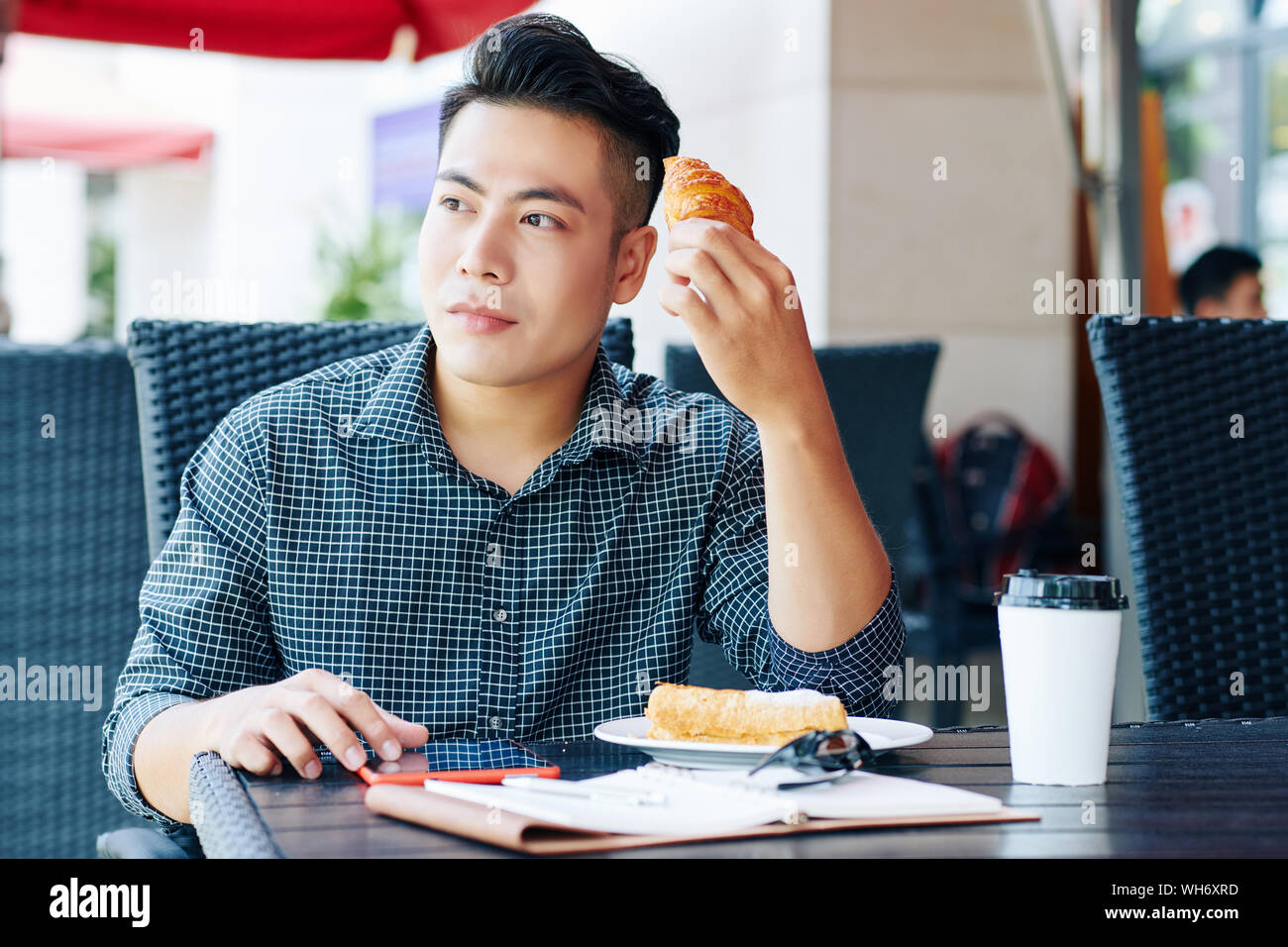 Portrait of handsome pensive young Vietnamese man eating pastries and ...