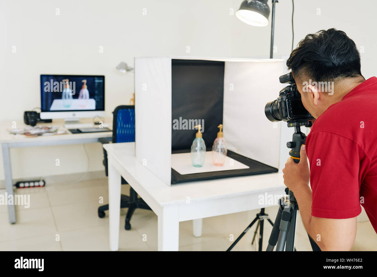 Photographer taking photos of glass bottles in light cube with black ...
