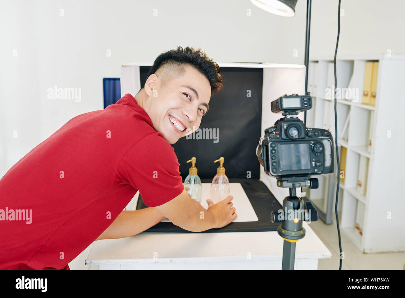 Happy young Asian man putting glass soap dispensers against black ...