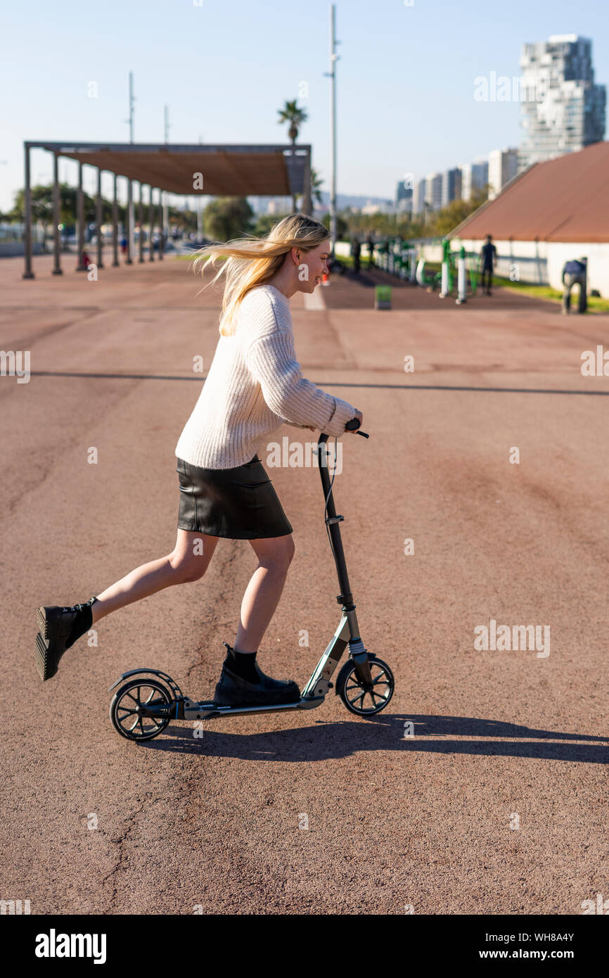 Smiling young woman riding kick scooter Stock Photo - Alamy