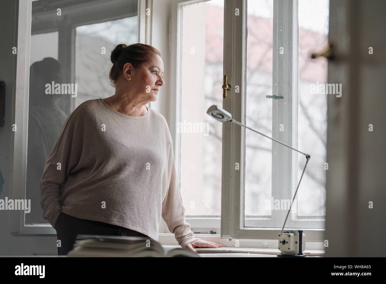 Serious senior woman looking out of window at home Stock Photo - Alamy