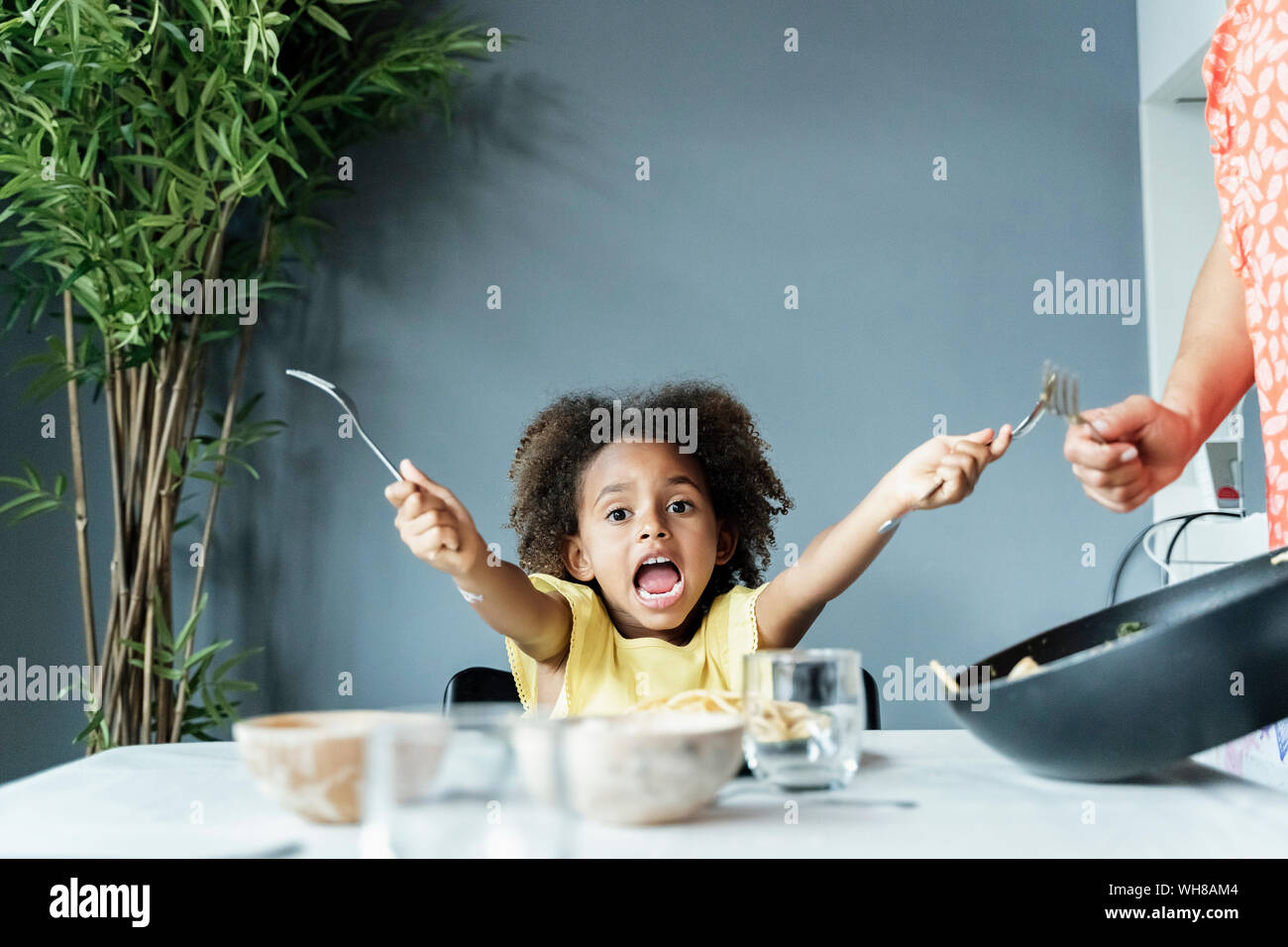 Portrait of cheering girl with mother serving meal at dining table ...