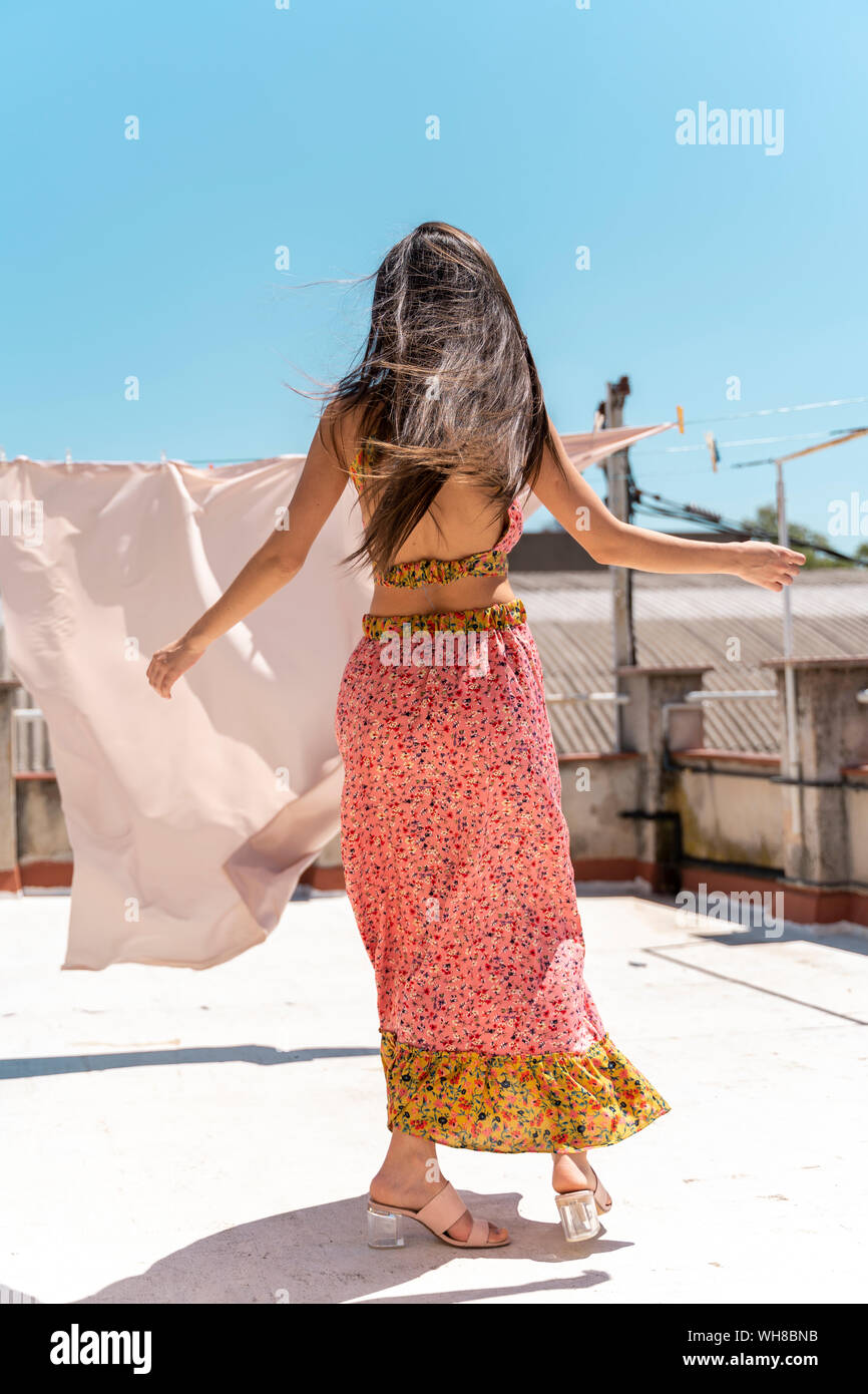Back view of woman wearing fashionable top and skirt dancing on roof ...