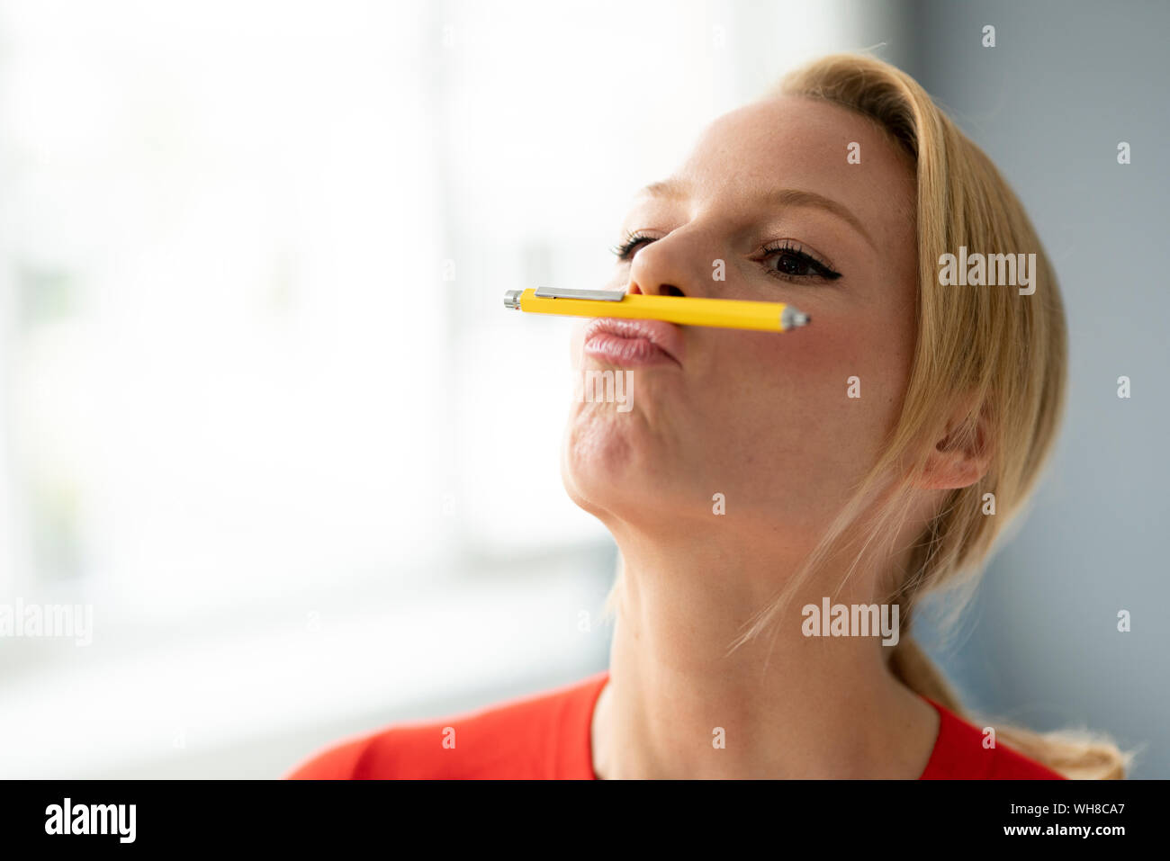 Playful young woman balancing pen on her mouth in office Stock Photo ...
