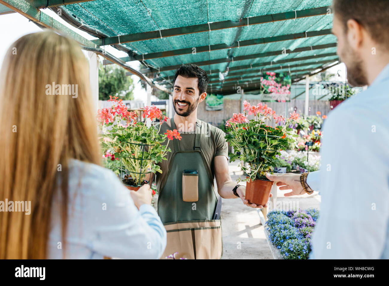 Happy worker in a garden center showing plants to customers Stock Photo ...