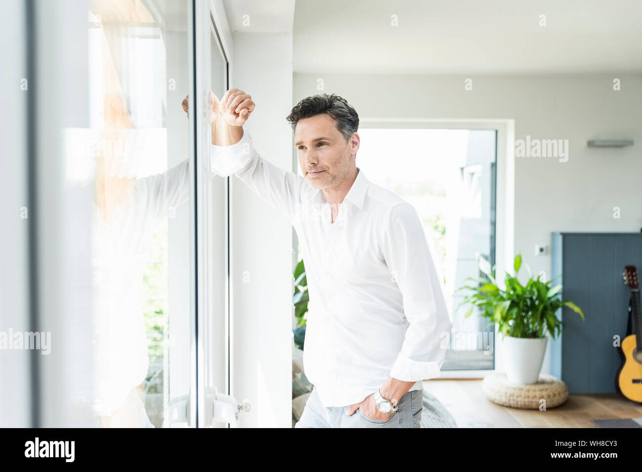 Serene man leaning on window at home Stock Photo - Alamy