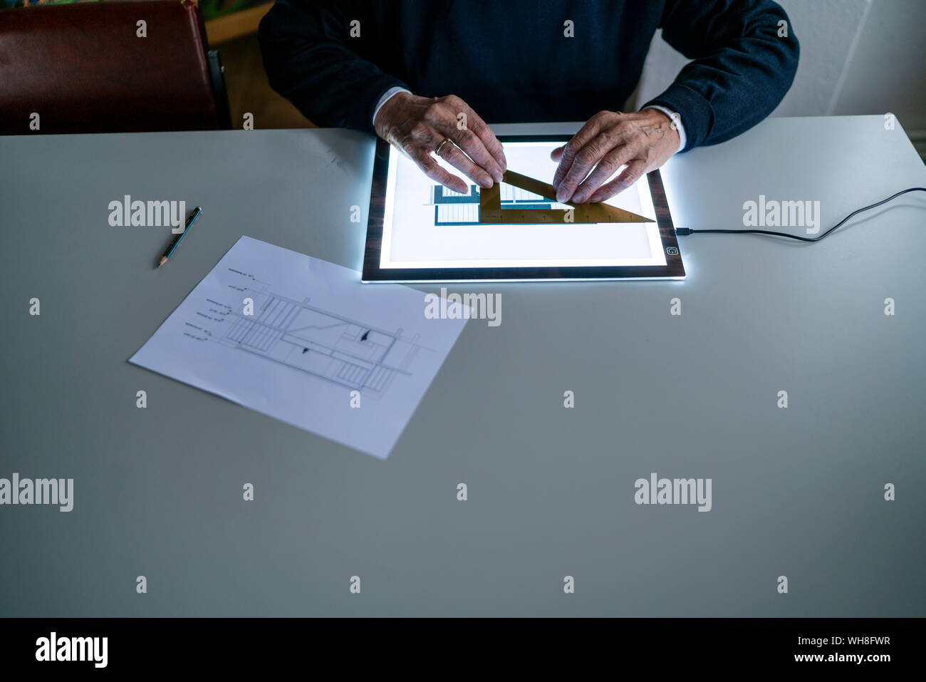 Close-up of senior man using ruler and tablet with architectural plan ...