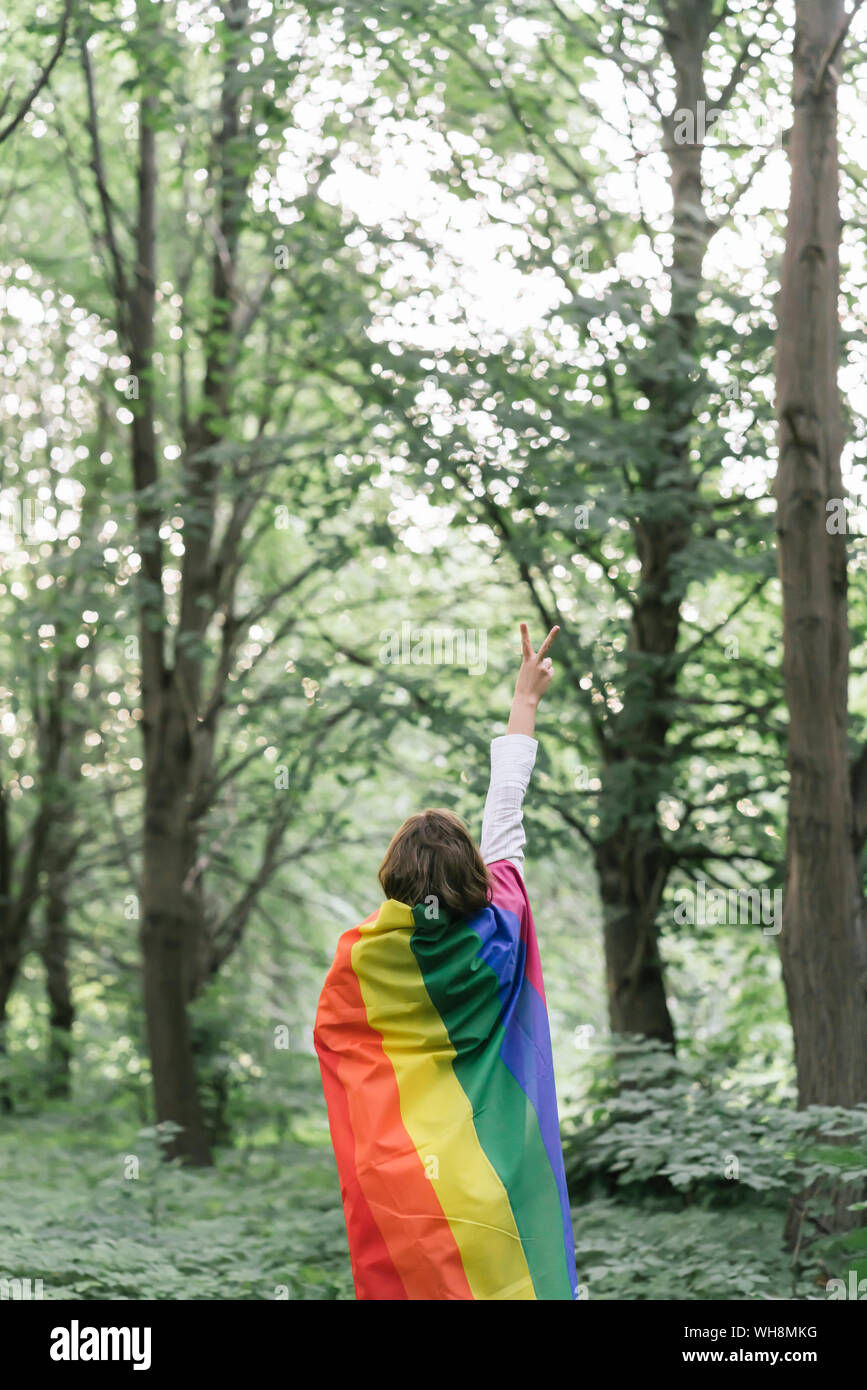 Rear view of a woman covered in a rainbow flag showing the victory sign ...