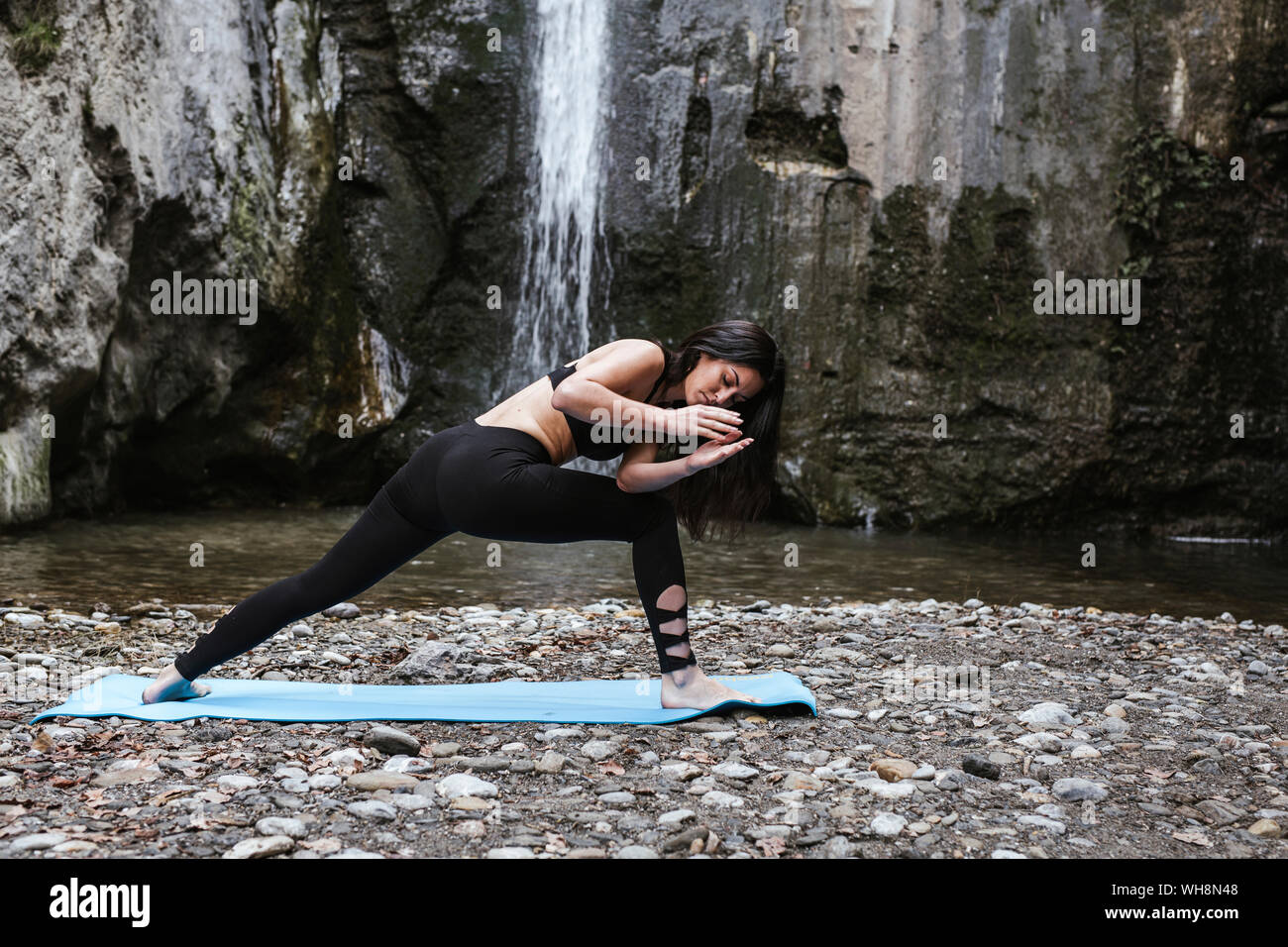Woman practising yoga at waterfall, triangle pose Stock Photo - Alamy