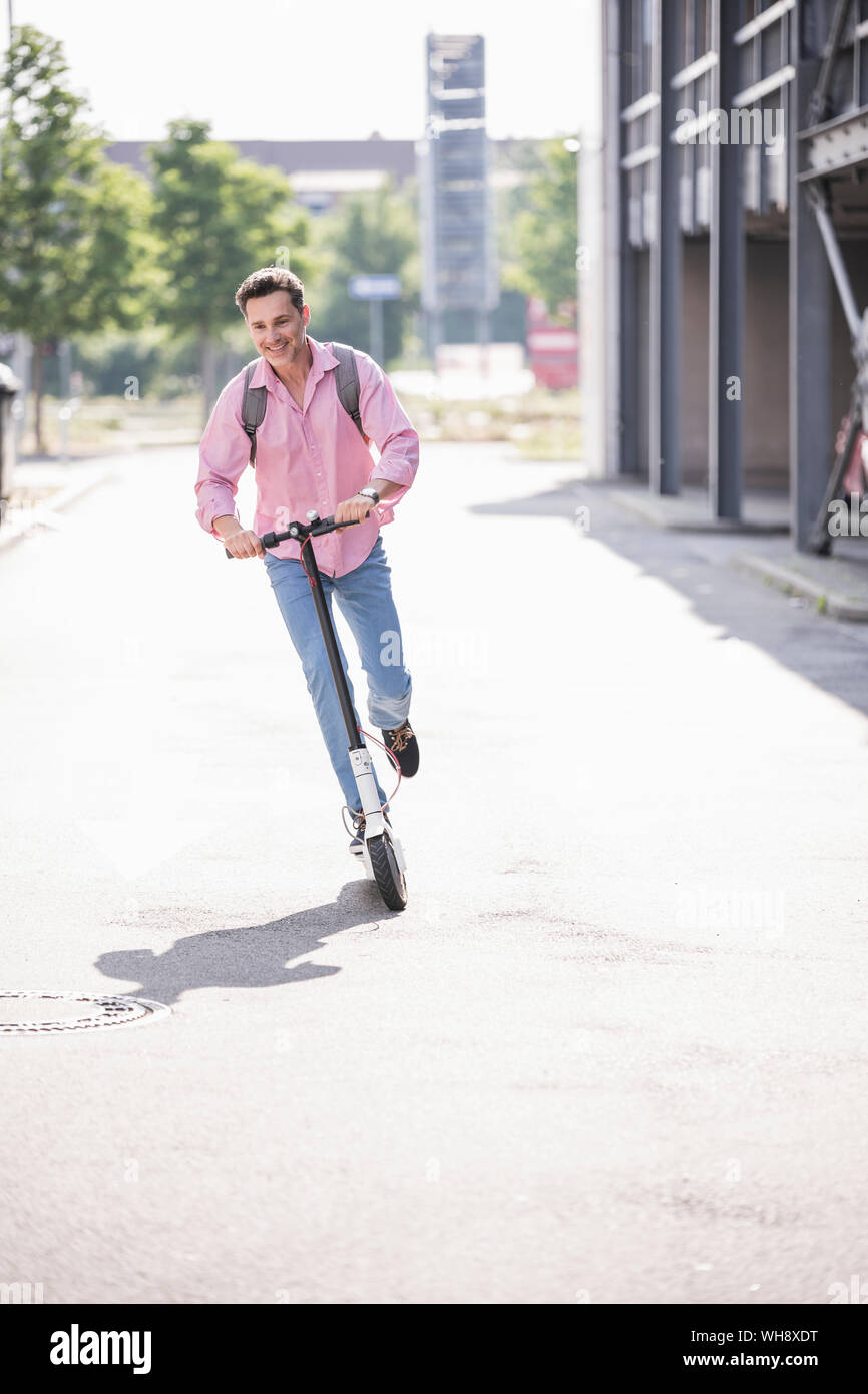 Businessman with backpack riding his E-Scooter Stock Photo - Alamy