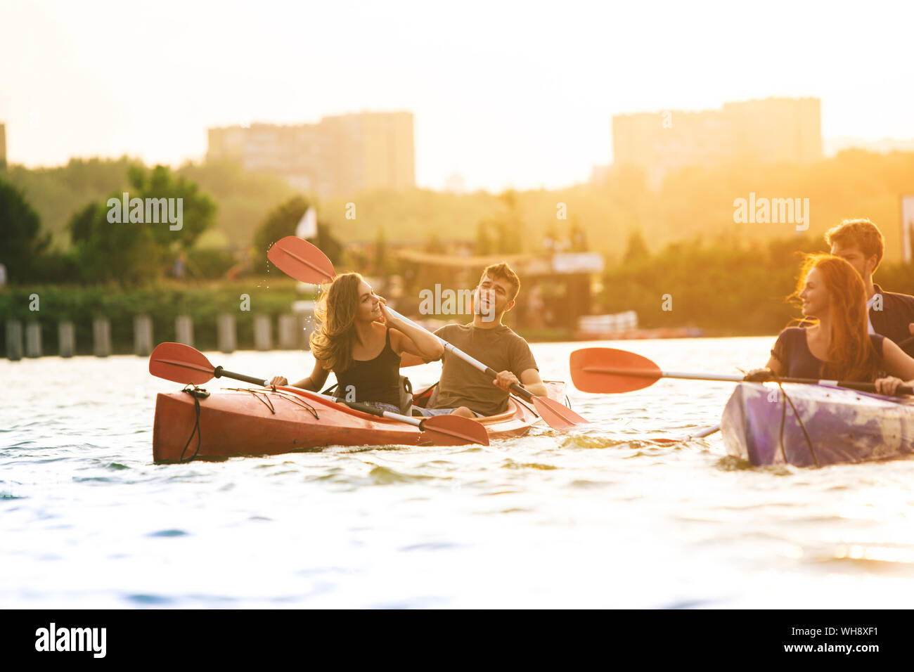 Happy young caucasian group of friends kayaking on river with sunset in ...