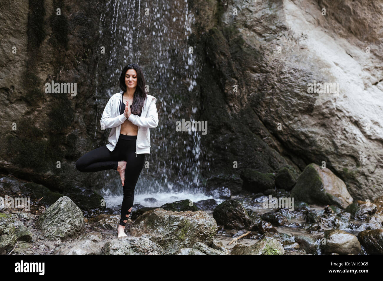 Woman practising yoga at waterfall, tree position Stock Photo - Alamy