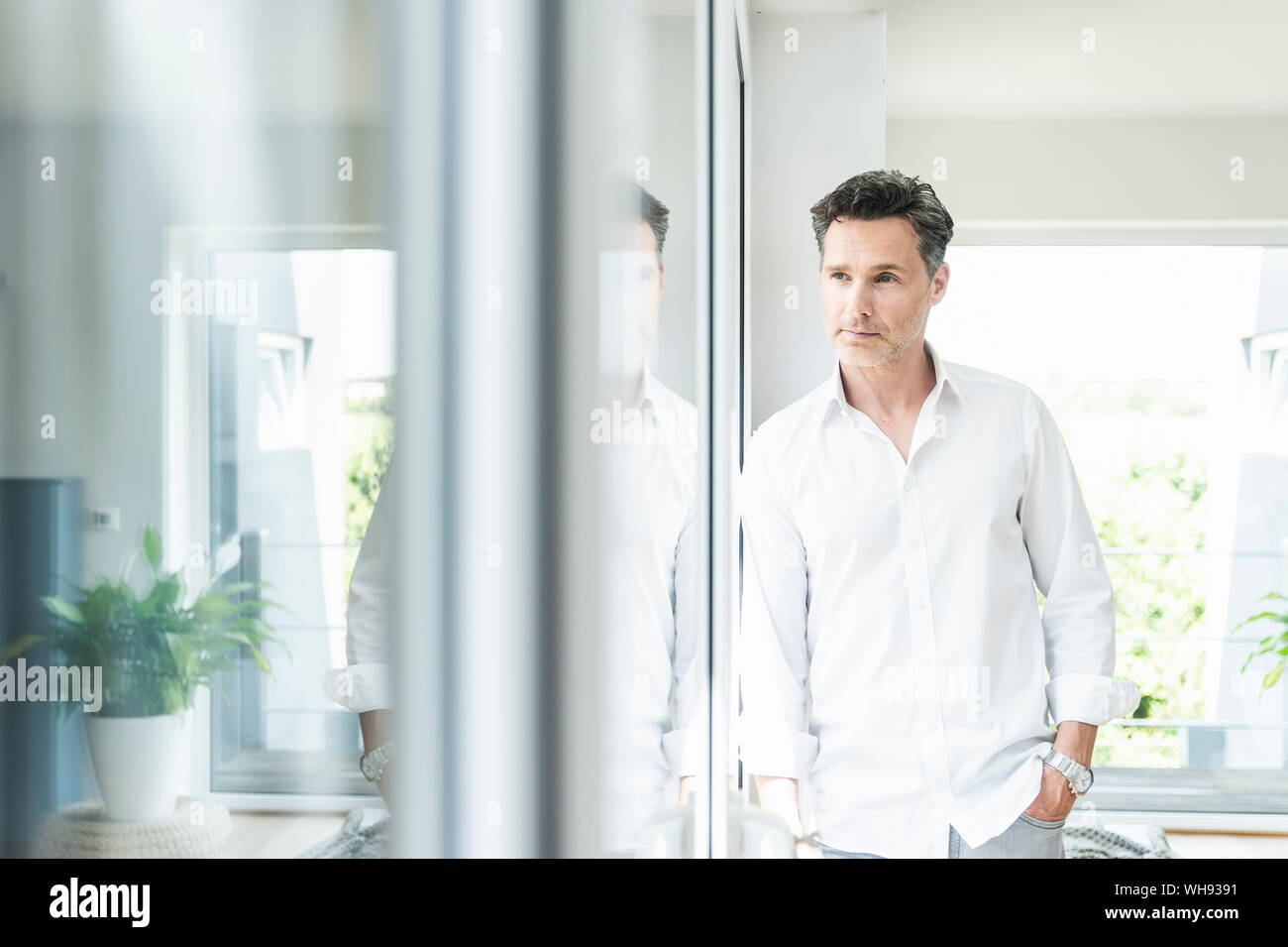 Serene man leaning on window at home Stock Photo - Alamy