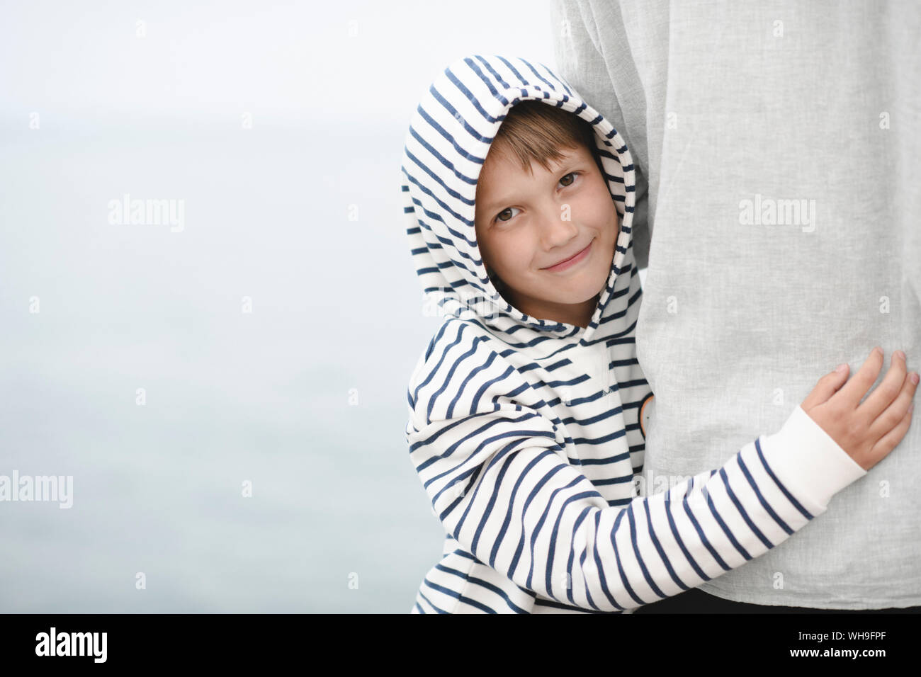 Portrait of smiling boy wearing striped hooded jacket hugging his ...