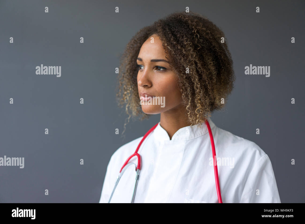 Portrait of young doctor with stethoscope in front of grey background ...