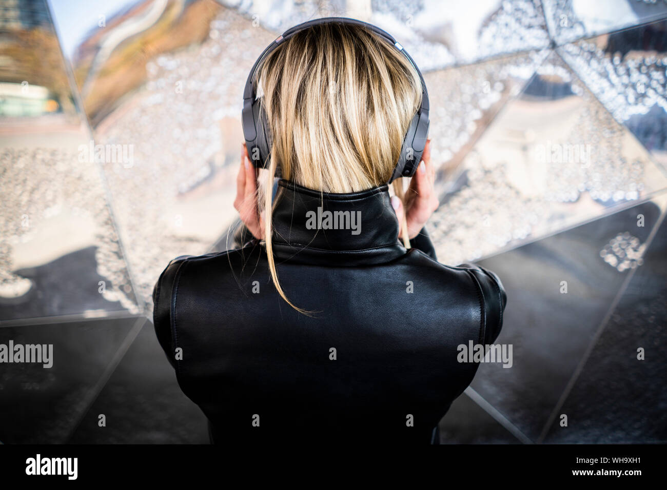 Back view of blond young woman listening music with wireless headphones ...