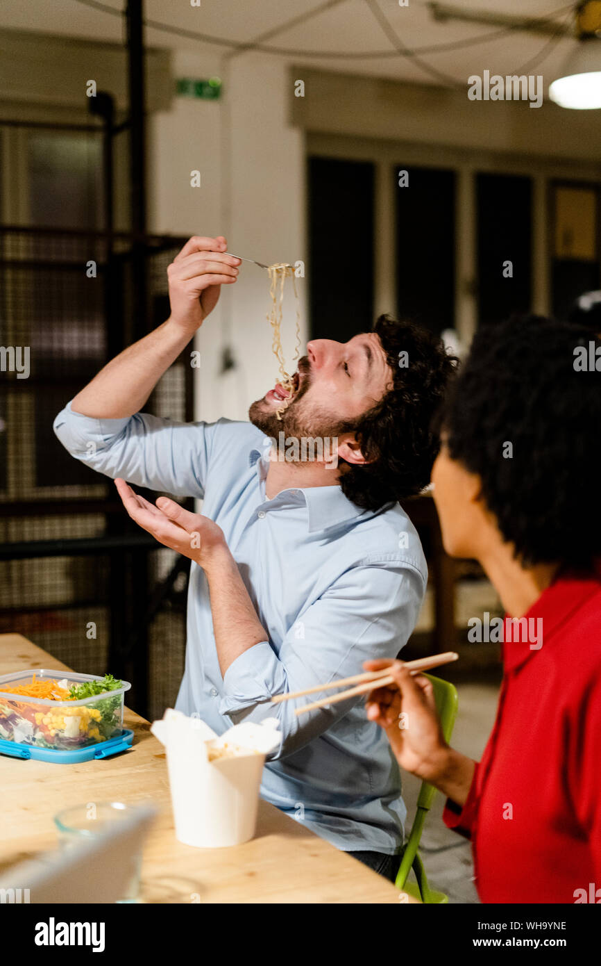 Businesswoman watching colleague eating noodles during lunch break ...