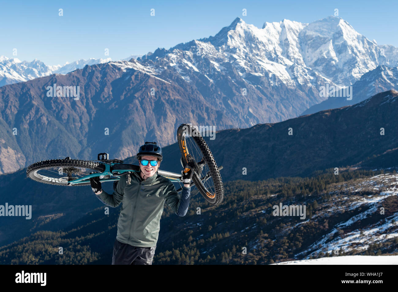 A mountain biker carries his bike up in the Himalayas with views of the ...