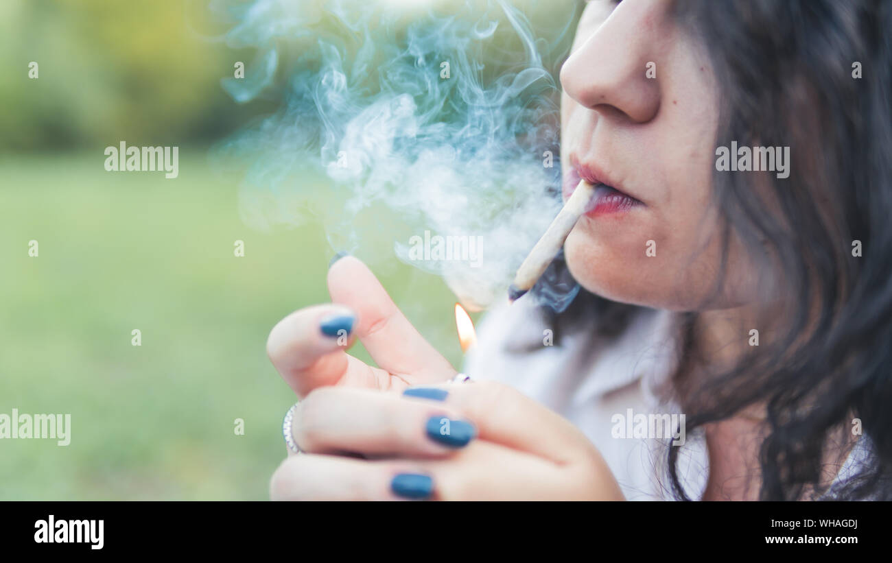 Girl smoking medical marijuana joint outdoors. The young women smoke cannabis blunt, close-up ...