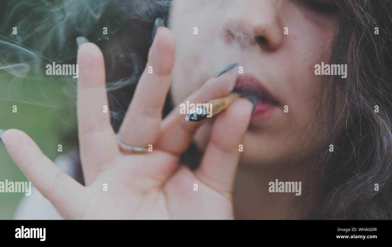 Girl smoking medical marijuana joint outdoors. The young women smoke cannabis blunt, close-up ...